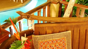 Uma área junto à piscina com um deque de madeira, espreguiçadeiras, uma piscina pequena e uma planta decorativa.