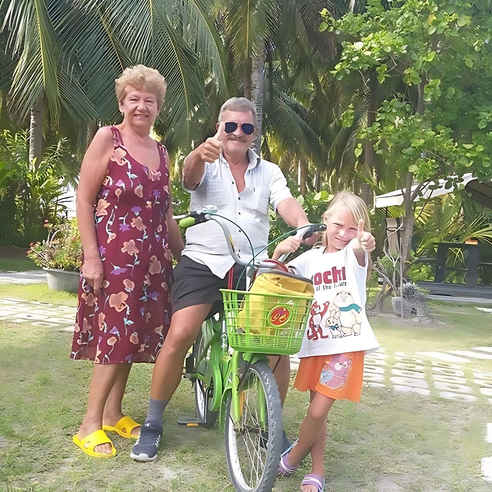 Uma família num triciclo verde com cesto, em um jardim com palmeiras.