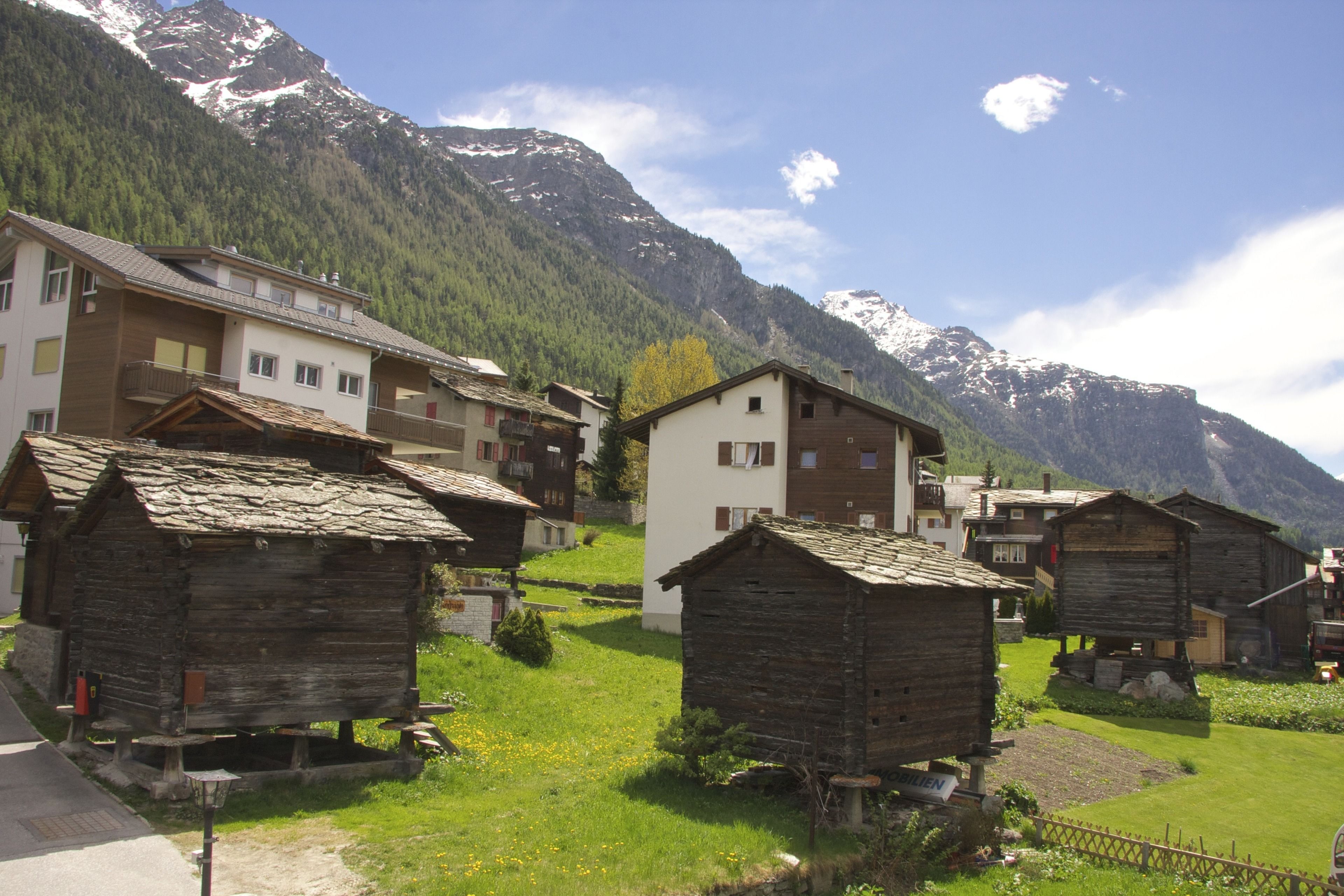 Uma aldeia de montanha tradicional com casas de madeira e montanhas cobertas de neve ao fundo.