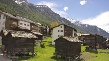 Uma aldeia de montanha tradicional com casas de madeira e montanhas cobertas de neve ao fundo.