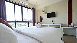 Quarto de hotel com uma cama grande, uma escrivaninha com televisão de tela plana, um espelho e uma janela com cortinas.