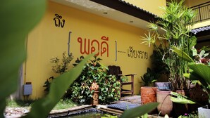 Paredes amarelas com escrita tailandesa e um pequeno elemento decorativo de água com plantas.