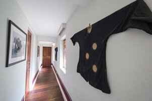 Um corredor com piso de madeira, quadros nas paredes e uma peça de roupa preta pendurada à direita.