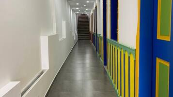 Um corredor comprido e estreito, com paredes brancas e chão coberto por azulejos cinzentos.