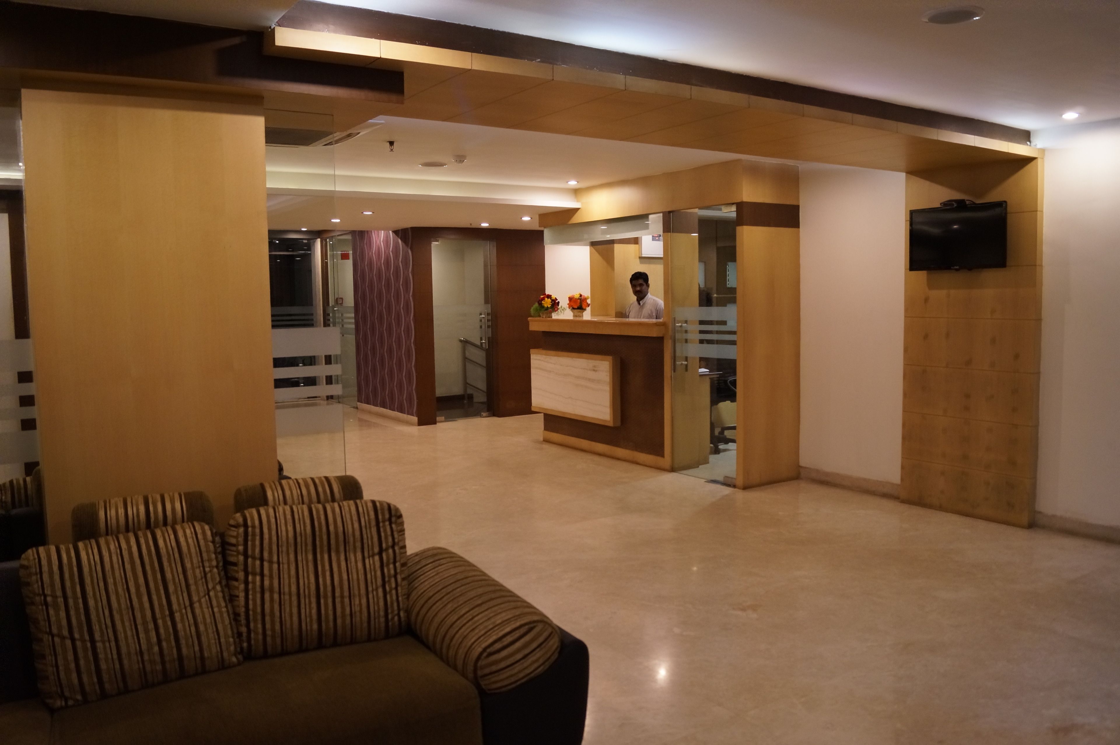 Um saguão de hotel com uma mesa de recepção, um sofá e uma TV fixada na parede.