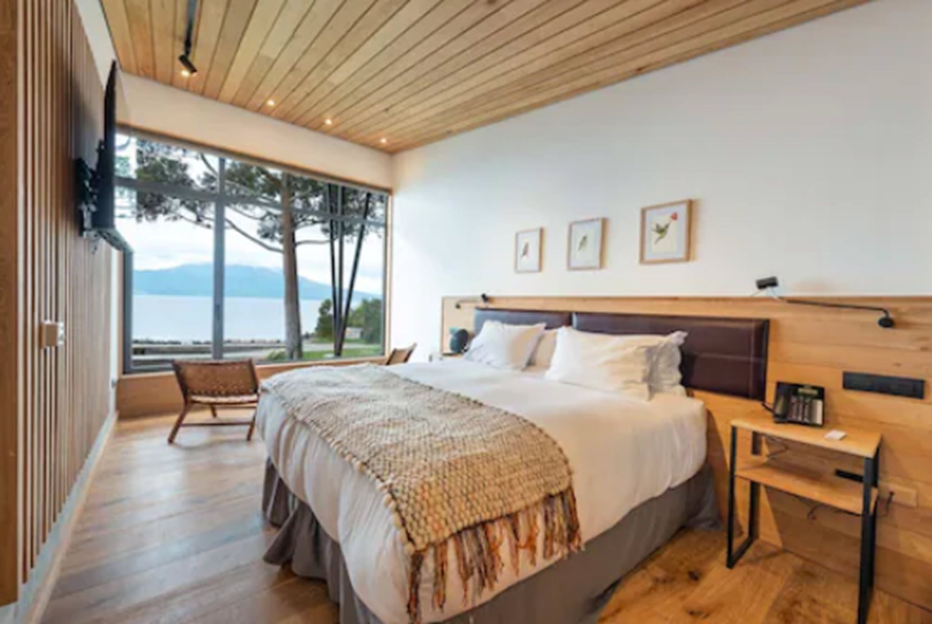 Um quarto moderno com uma cama grande, cabeceira de madeira e vista para um lago.