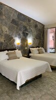 Quarto de hotel com duas camas, paredes de pedra e vista para o exterior.