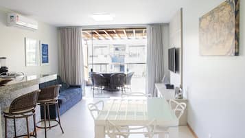 Uma sala de estar moderna com uma mesa de jantar de vidro, dois bancos altos, um sofá e uma televisão em um móvel.