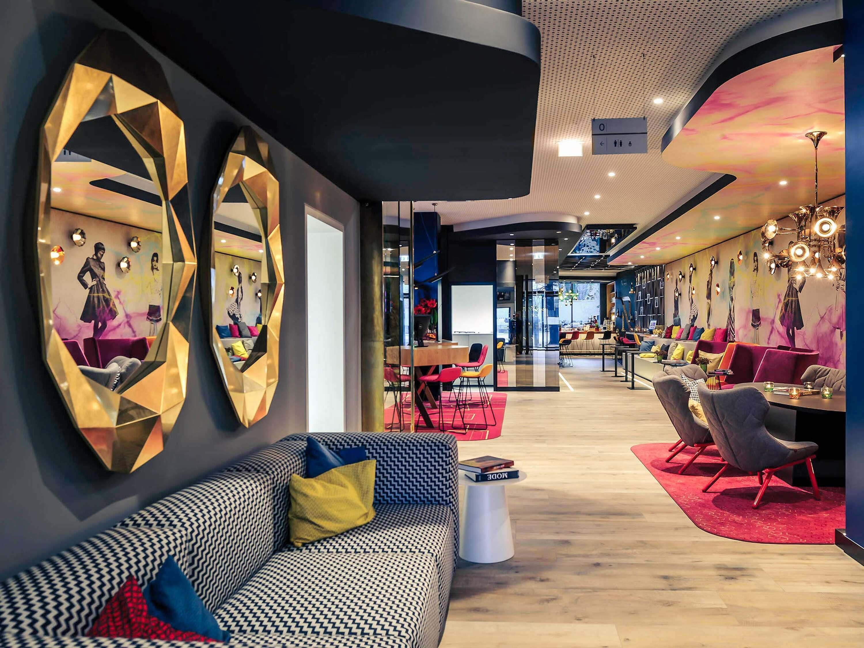 Um lobby de hotel moderno com área de estar central, um bar e uma escadaria para um andar superior.