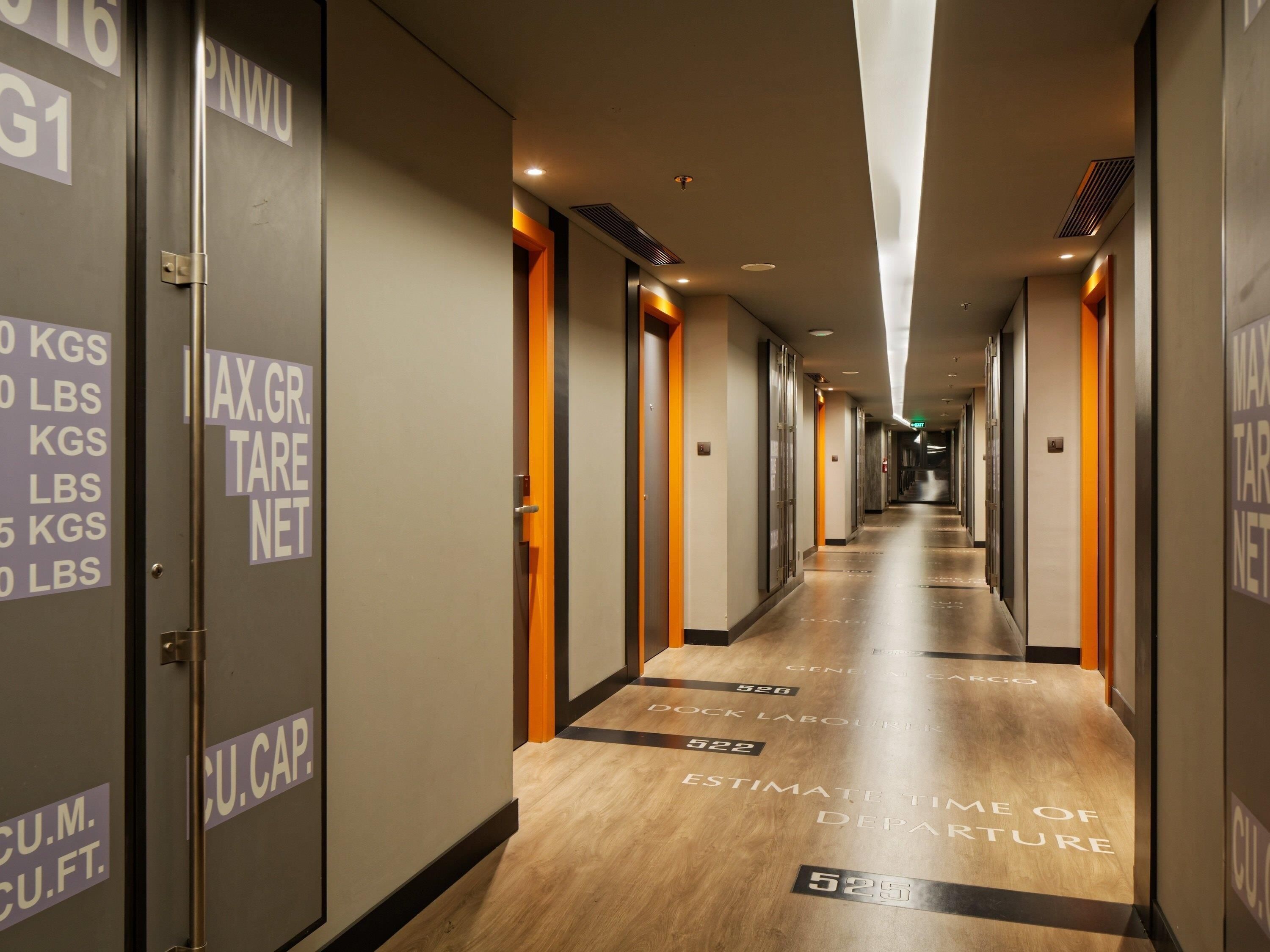 Corredor de hotel com portas identificadas por números de quarto e limites de peso.