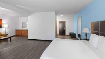 Quarto de hotel com uma cama grande, uma escrivaninha, uma cadeira, um sofá e uma pequena cozinha.