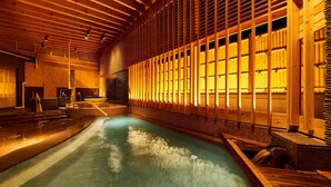 Uma onsen japonesa tradicional com interior em madeira, uma nascente termal central e uma parede de azulejos com padrão quadriculado.