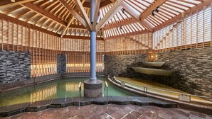 Uma área de spa com banheira de hidromassagem, paredes de pedra, vigas de madeira e piso ladrilhado.