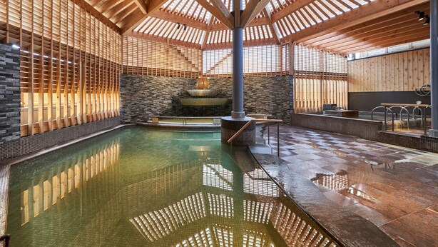 Um spa com uma grande piscina interior, vigas de madeira, paredes de pedra e uma lareira de pedra.