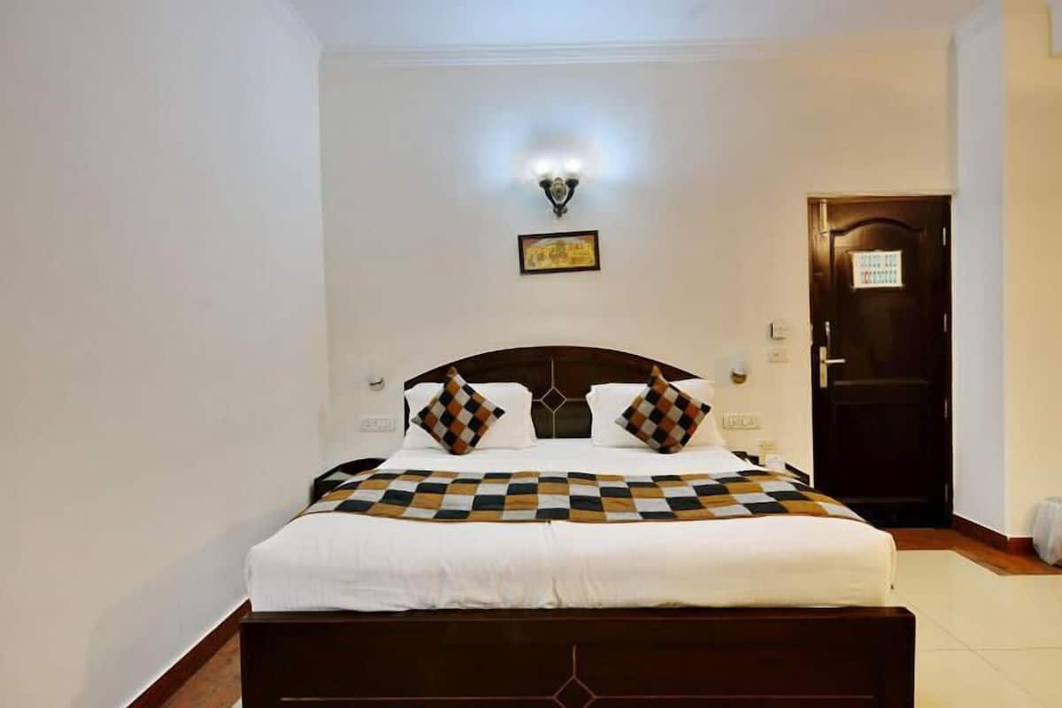 Cama bem arrumada com colcha xadrez e duas almofadas decorativas, luminária fixada na parede e um quadro emoldurado acima da cama.