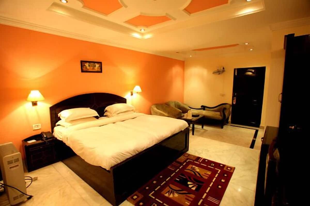 Quarto de hotel com cama, duas luminárias de cabeceira, uma cadeira, uma mesa e uma porta.