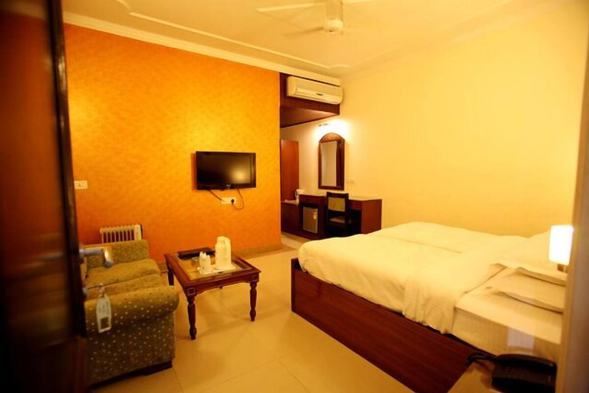 Quarto de hotel com cama, um pequeno sofá, mesa de cabeceira com amenities, TV fixada na parede e ar condicionado.