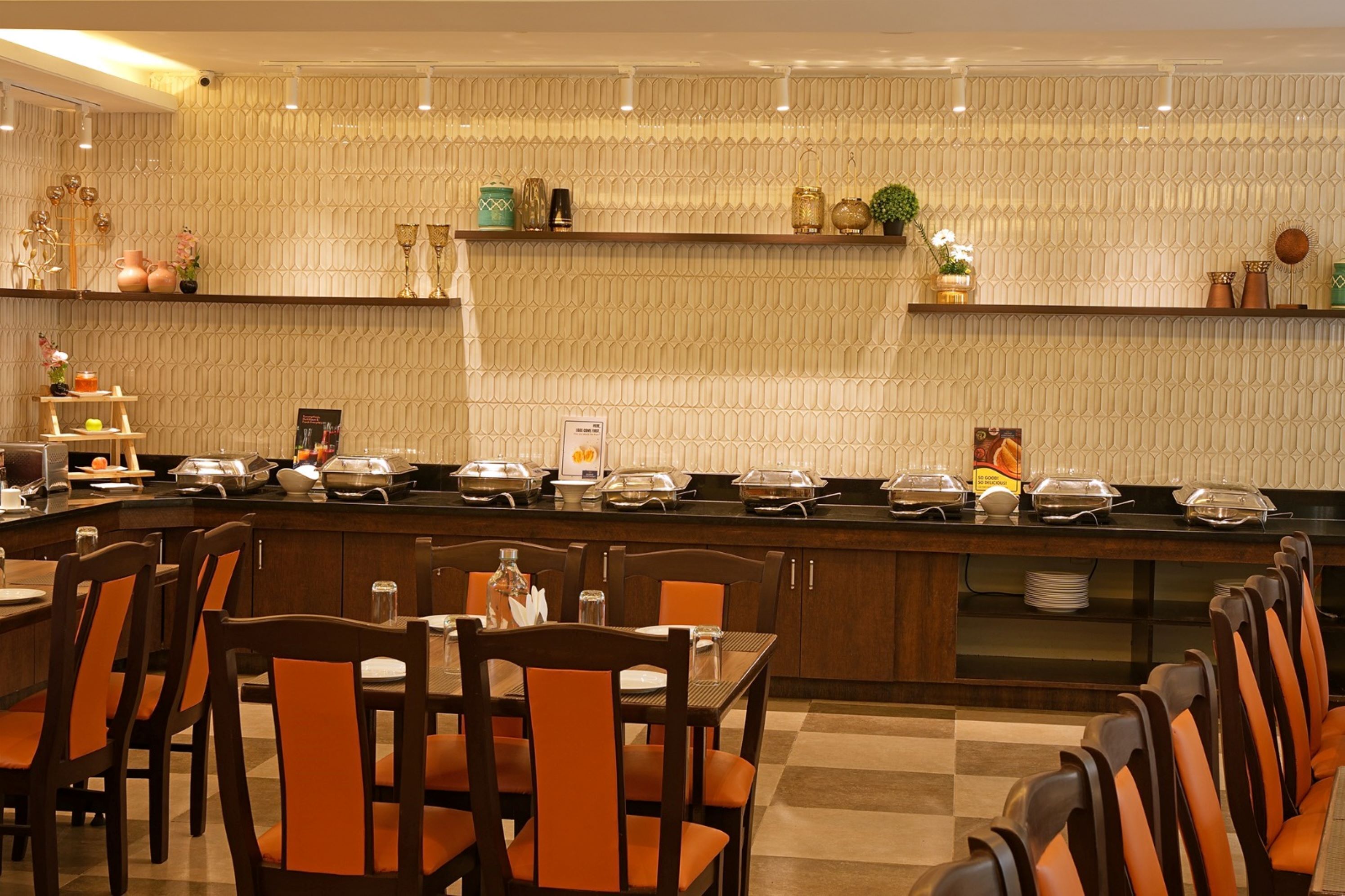 Disposição de buffet com várias estações de serviço, cadeiras de madeira e parede estampada.