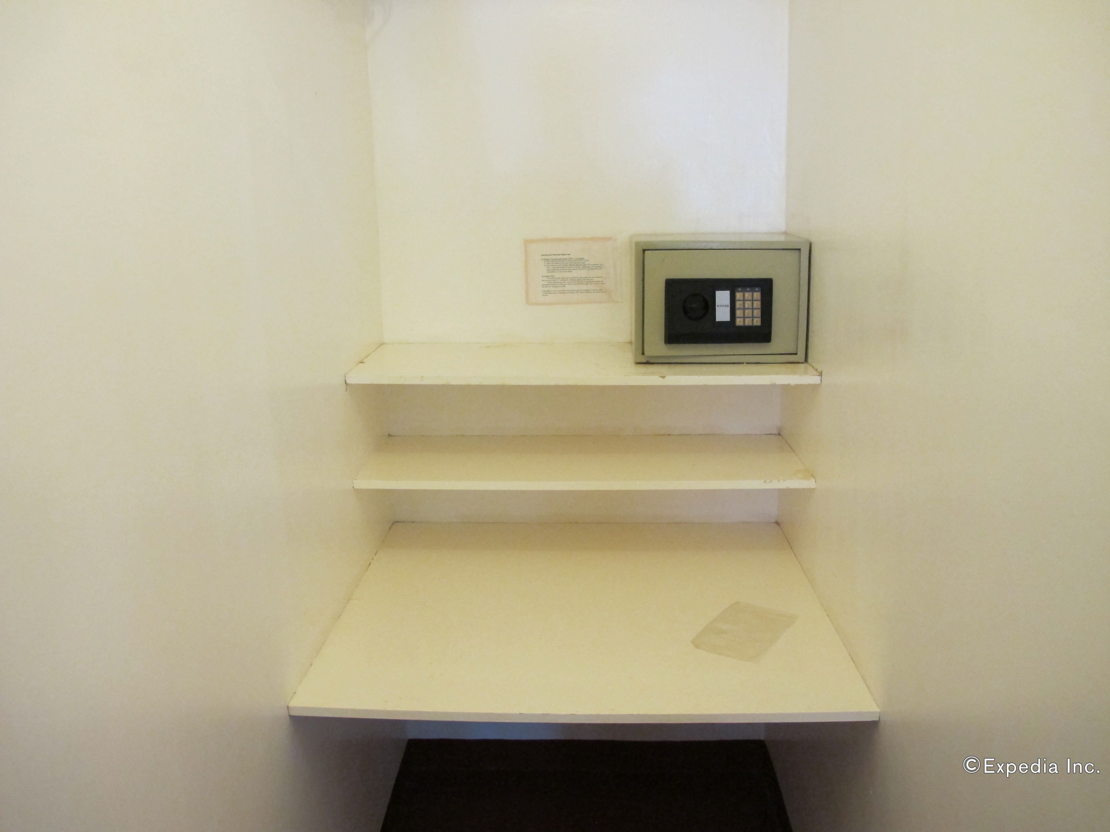 Quarto branco com três prateleiras, e um cofre pequeno na prateleira de cima.
