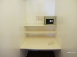 Quarto branco com três prateleiras, e um cofre pequeno na prateleira de cima.
