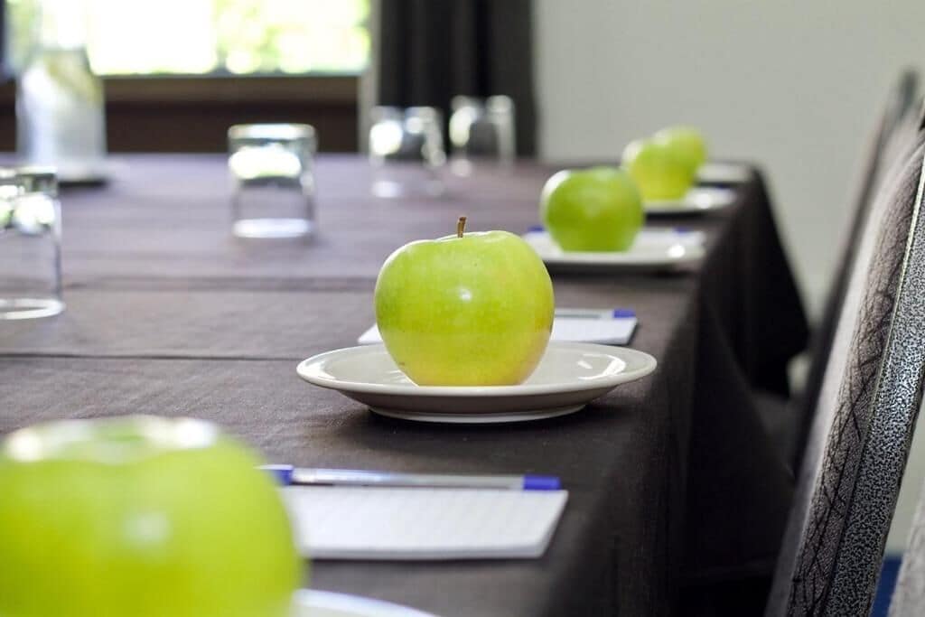 Uma mesa de conferência com pratos de maçãs verdes, copos e um bloco de notas.