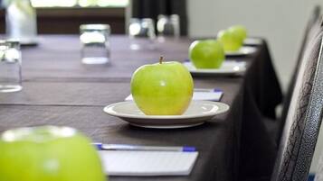 Uma mesa de conferência com pratos de maçãs verdes, copos e um bloco de notas.