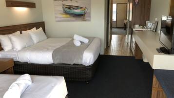 Quarto de hotel com cama, escrivaninha, televisão e pintura de um barco.
