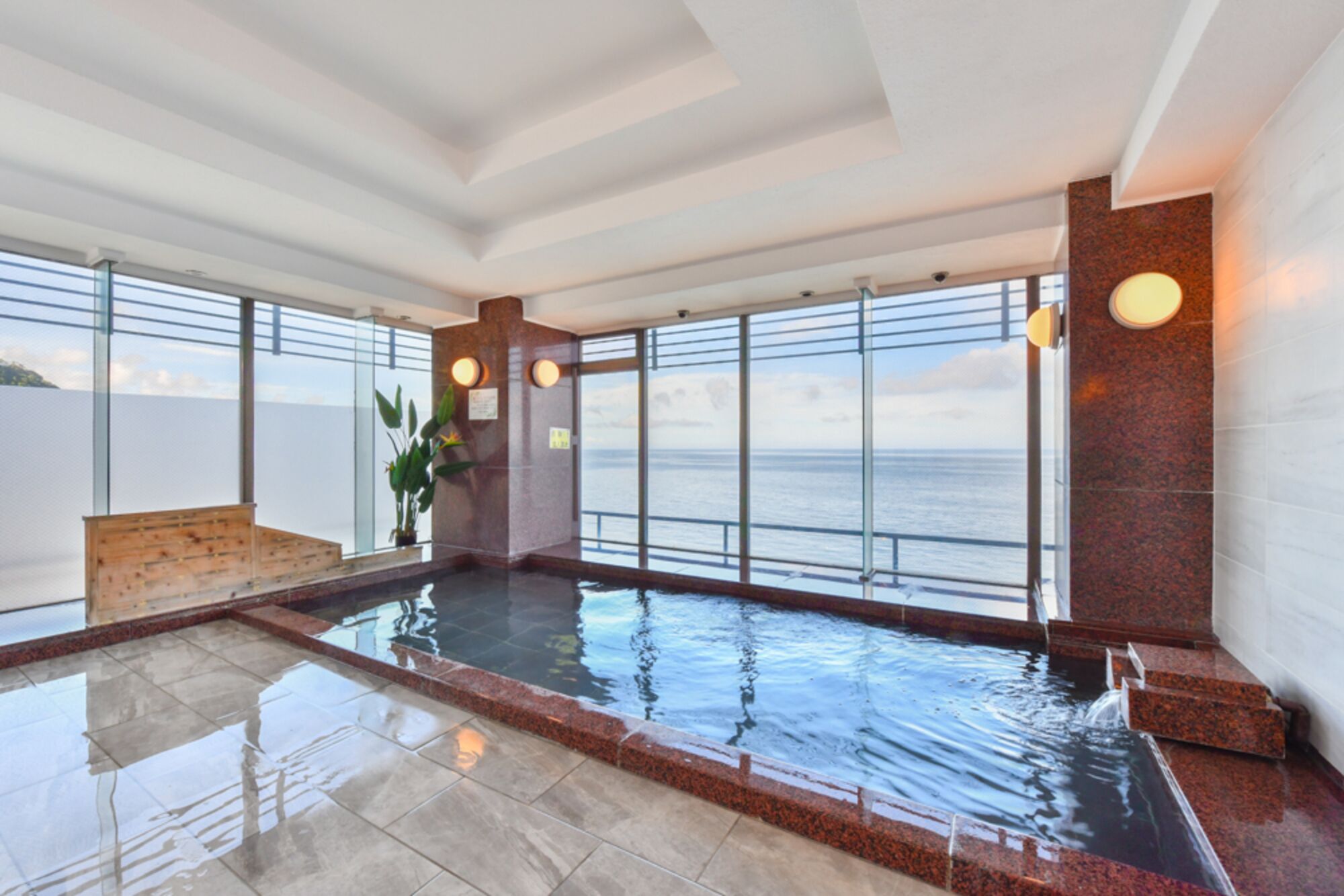 Piscina interna com vista para o mar, um banco de madeira e um vaso de planta.