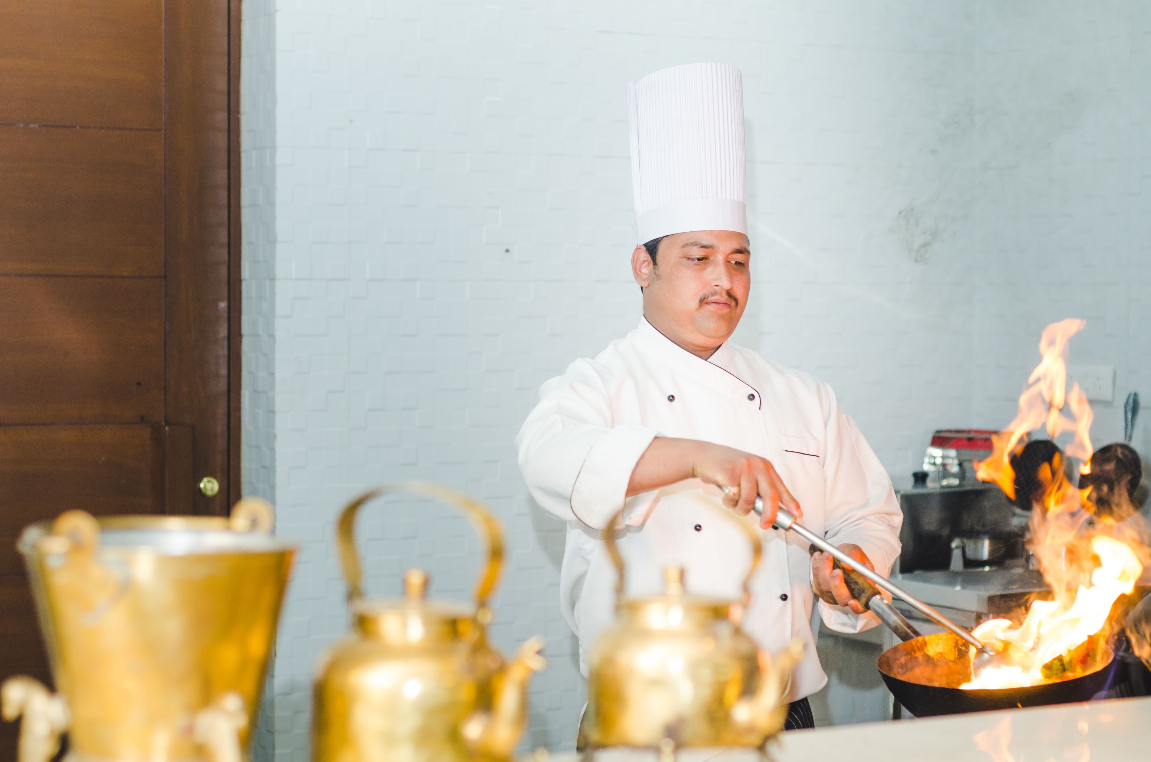 Um cozinheiro com uniforme branco cozinhando com um wok sobre chama aberta.