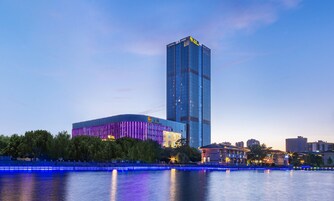 Um edifício moderno com fachada de vidro refletiva e uma construção menor com iluminação roxa na frente.