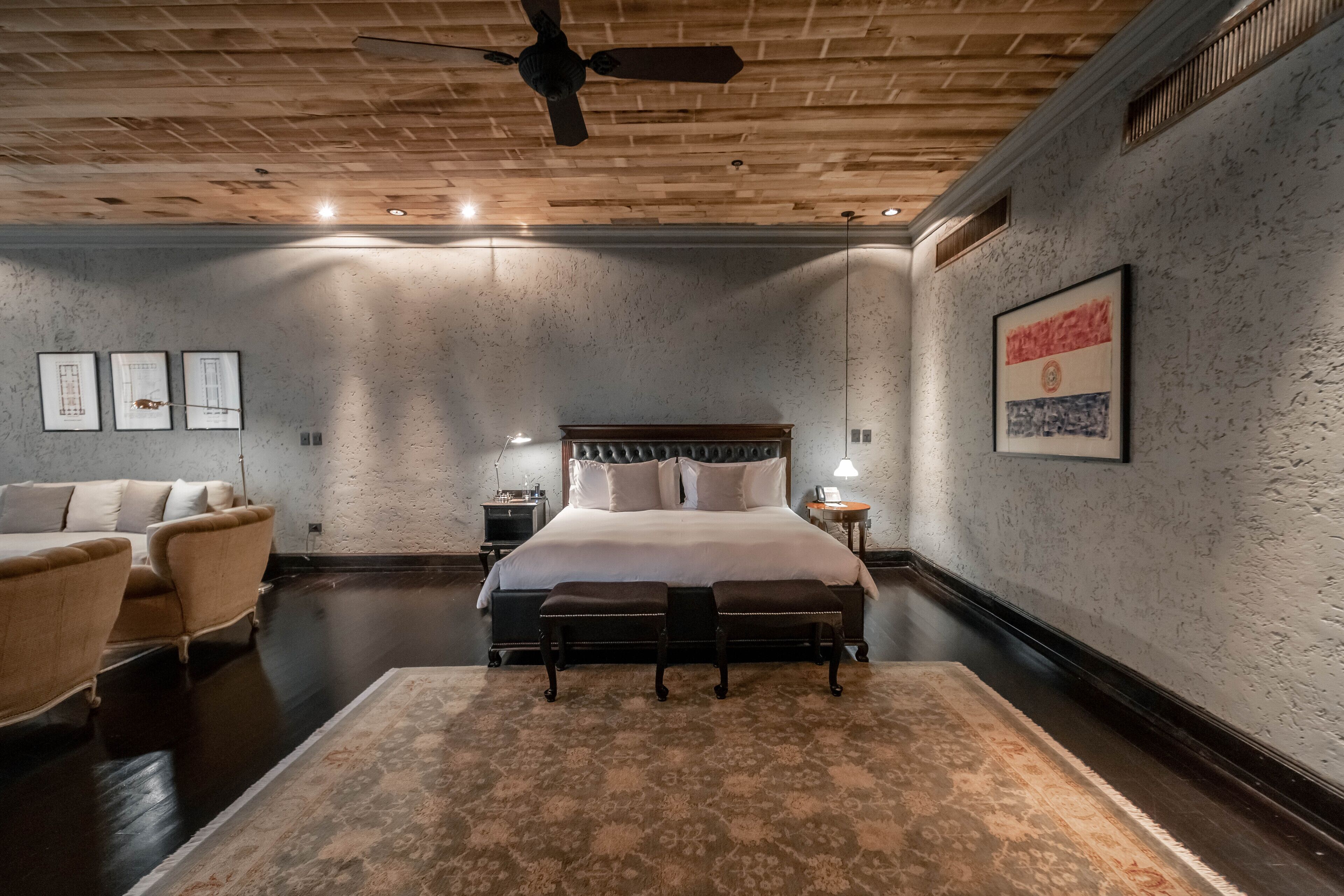 Um quarto espaçoso com uma cama grande, um ventilador de teto e uma bandeira emoldurada na parede.