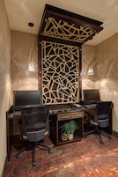 Um espaço de escritório moderno com duas mesas, cada uma com um computador e uma cadeira, uma divisória de madeira decorativa e luminárias pendentes.