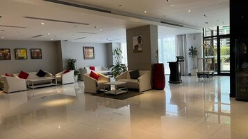 Um lobby moderno de hotel com piso limpo e brilhante, móveis contemporâneos e grandes janelas que permitem a entrada de luz natural.