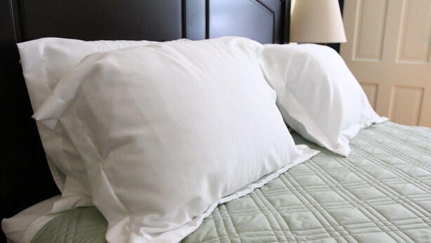 Uma cama com um edredom verde e almofadas brancas.