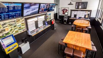 Uma sala de controle com vários monitores, uma mesa de madeira e banquetas.