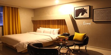 Quarto de hotel com cama, poltrona, mesa pequena com bebidas e obras de arte na parede.