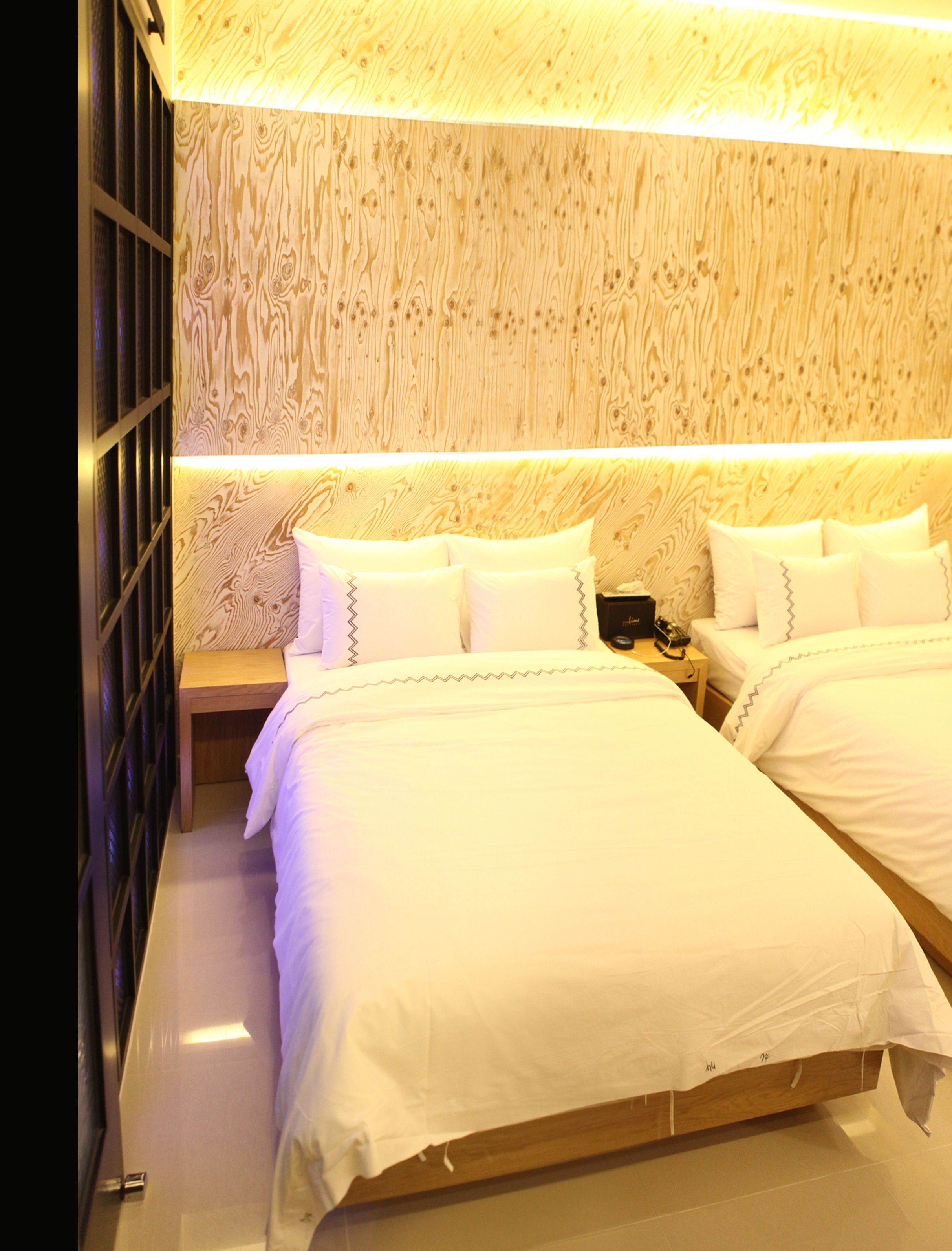 Quarto de hotel com duas camas, cabeceira de madeira, mesas de cabeceira e criado-mudo com telefone.