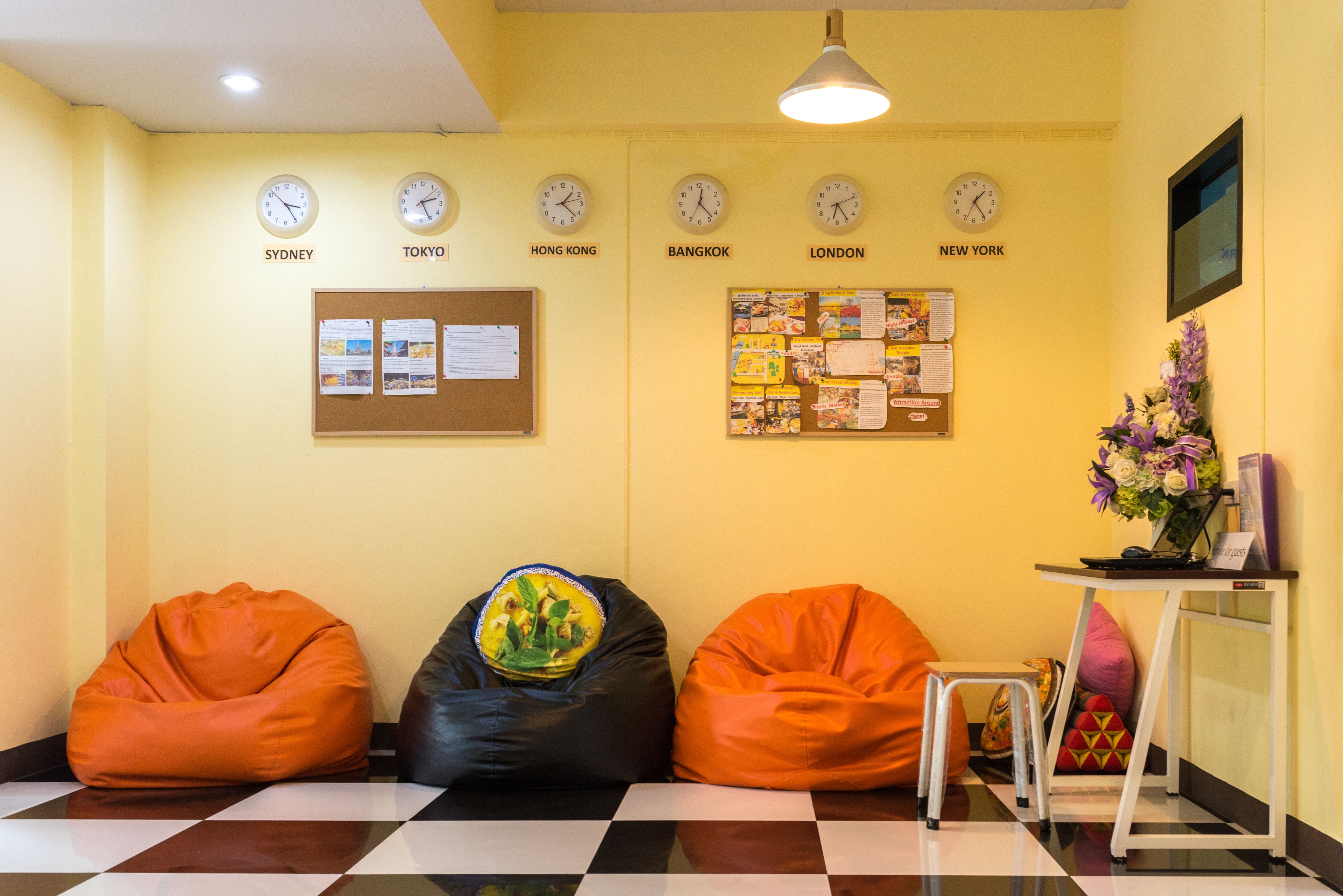 Uma área de recepção com poltronas de feltro, relógios exibindo horários de diferentes cidades, um mural de avisos e uma pequena mesa com um vaso de flores.