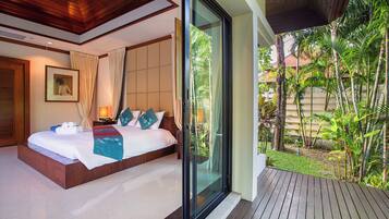 Quarto de hotel com uma cama grande, porta de vidro que dá para uma varanda e vista de vegetação tropical.