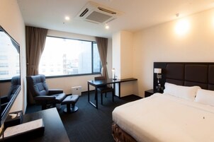 Quarto de hotel com cama, escrivaninha, cadeira e janela com cortinas.