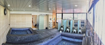 Uma área de spa moderna com duas banheiras de hidromassagem, um balcão de recepção e vista para a cidade através de grandes janelas.