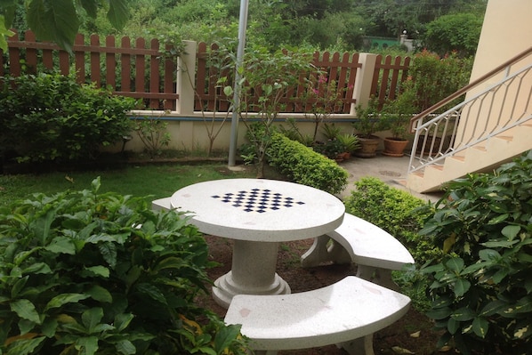 Um jardim com mesa xadrez, cerca de madeira e plantas em vasos.