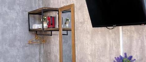 Quarto com escrivaninha de madeira, televisão de tela plana na parede, espelho e prateleira com diversos objetos.