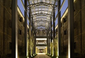 Uma galeria coberta com teto de vidro, ladeada por edifícios de tijolo e iluminada por luz artificial.