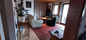 Uma sala de estar com sofá, poltrona, mesa de centro, televisão e uma planta grande em vaso.