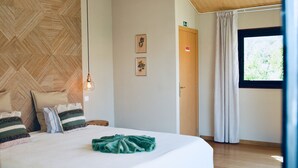Cama bem arrumada com almofadas estampadas, manta verde e cabeceira de madeira.