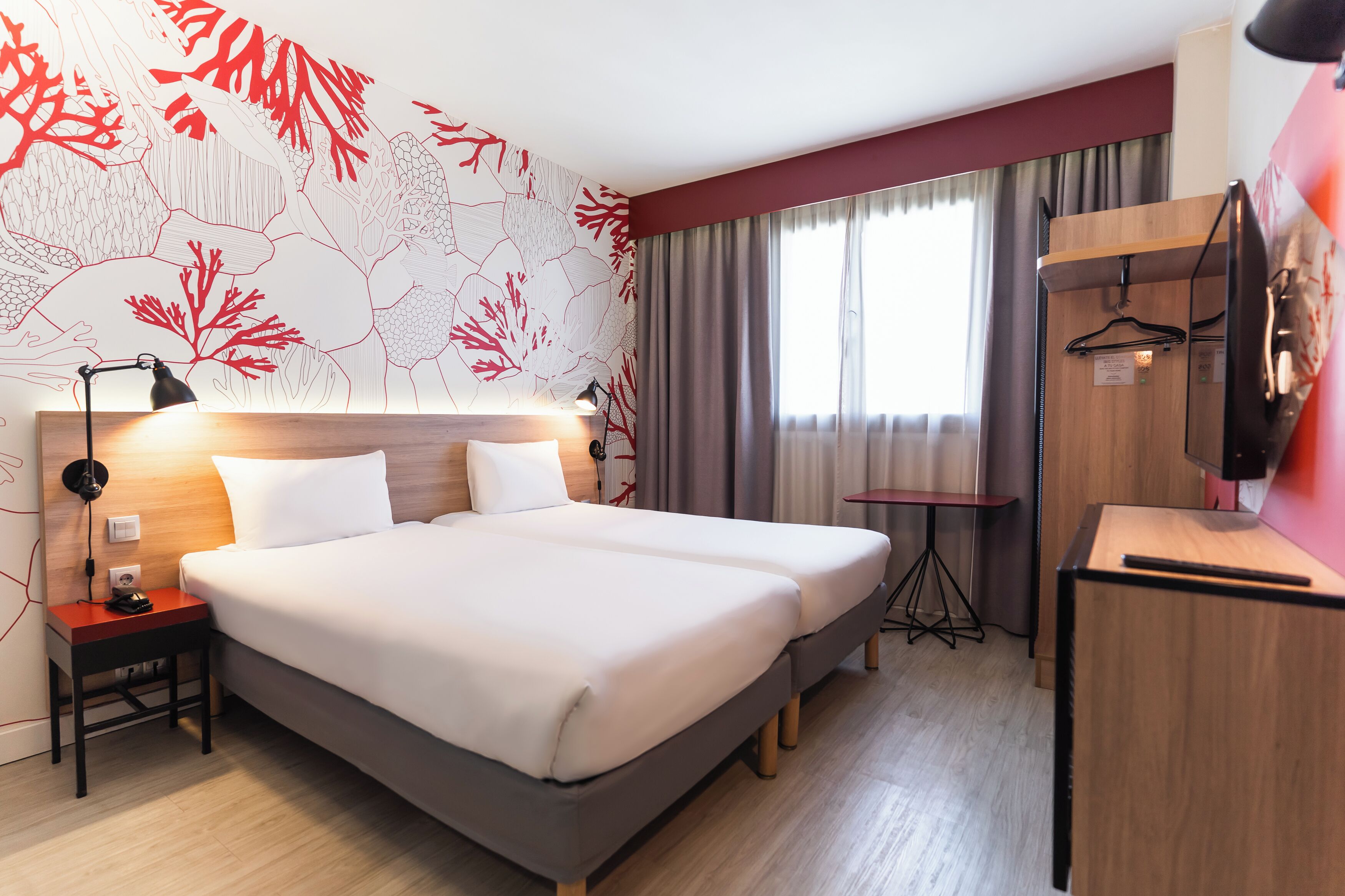 Quarto de hotel com cama grande, mesas de cabeceira, escrivaninha, televisão e janela com cortinas.
