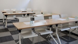 Sala de conferência com várias mesas e cadeiras, equipada com garrafas de água e papéis.