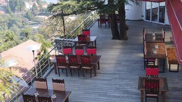 Um deck de madeira com mesas e cadeiras, com vista para uma colina com edifícios.