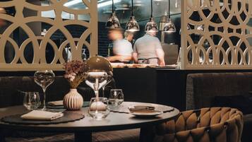 Interior de restaurante com uma mesa posta para dois, um vaso decorativo e uma taça de vinho.